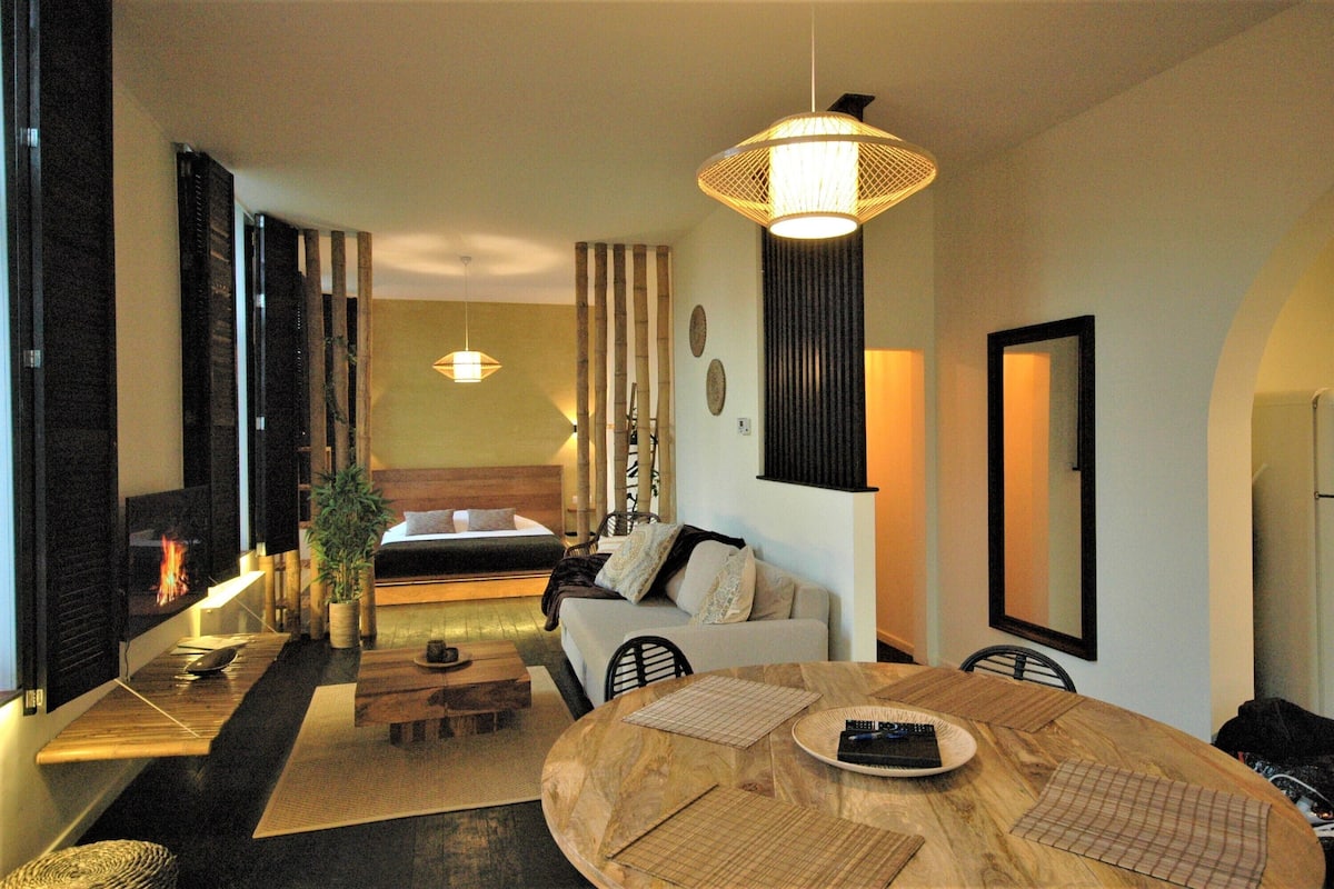 Quarto de hotel moderno com sofá, mesa de jantar, lareira e uma janela grande.