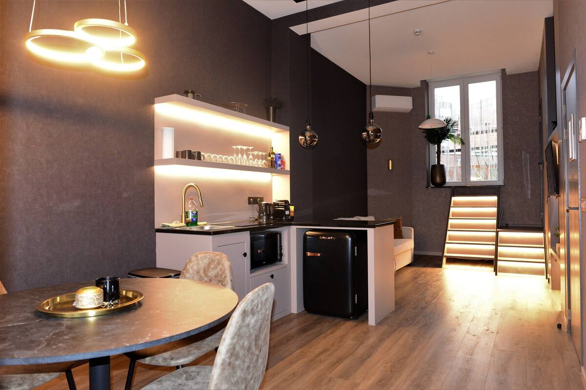 Cozinha moderna com geladeira embutida, área de jantar com mesa redonda e iluminação pendente.