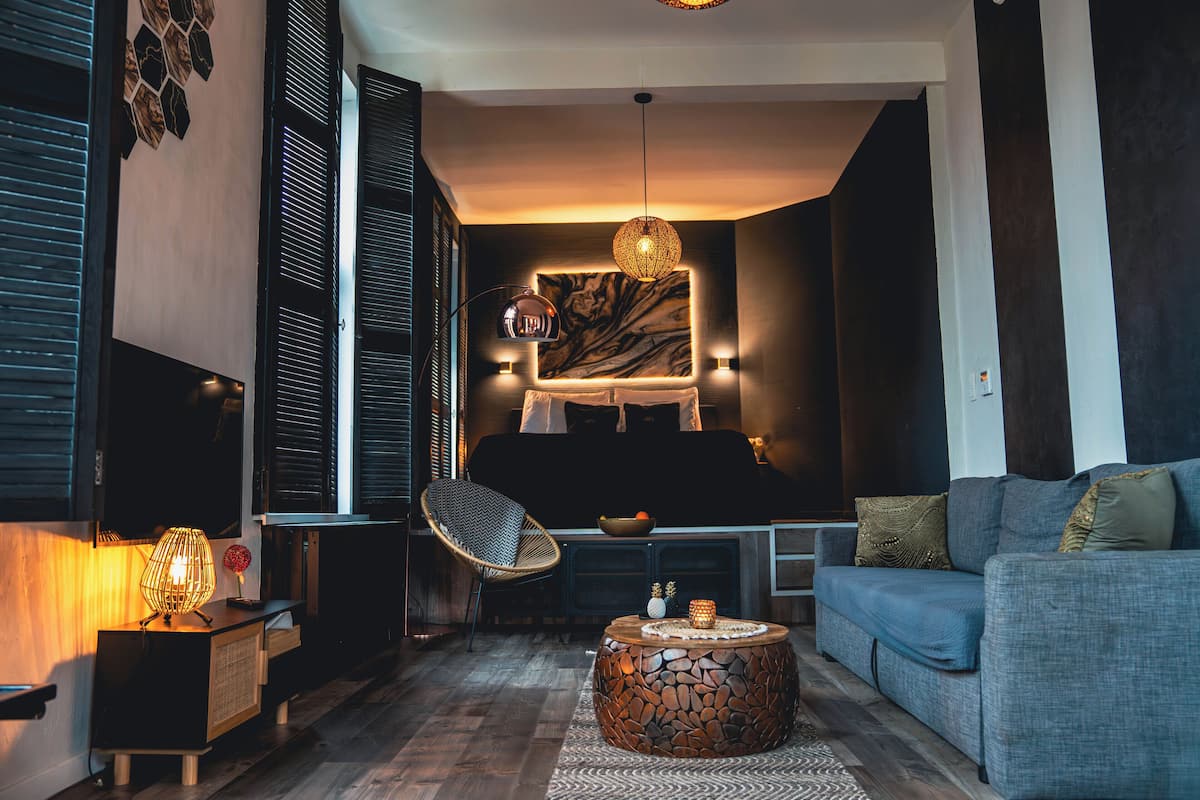 Uma sala de estar moderna com um sofá, uma mesa de centro redonda, uma poltrona e um candeeiro fixado na parede.