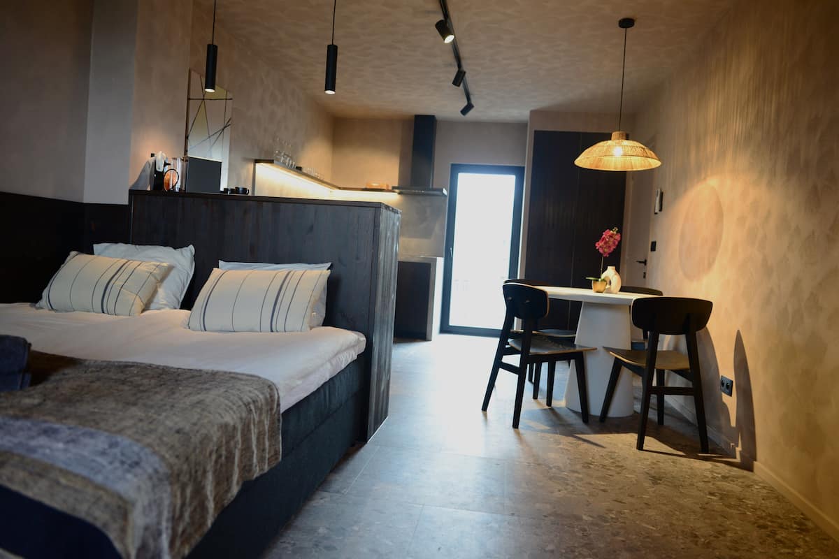 Quarto de hotel moderno com uma cama grande, uma escrivaninha e uma cadeira. Há um espelho acima da escrivaninha e um candeeiro suspenso.