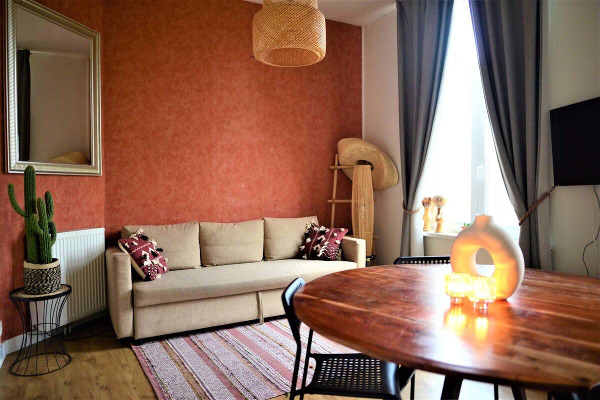 Uma sala de estar acolhedora com um sofá, uma mesa redonda de madeira e uma planta cacto.