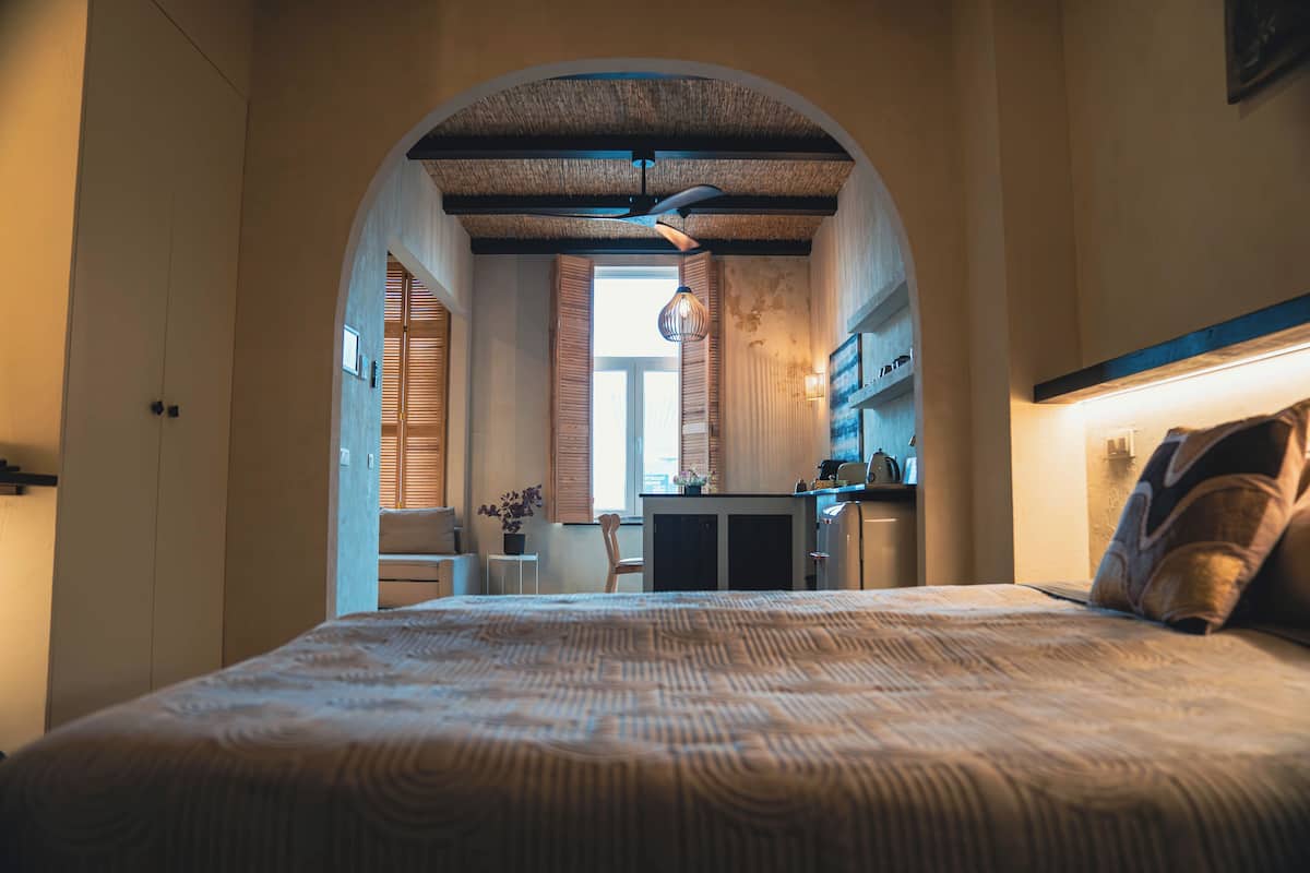 Quarto com uma cama grande, porta arqueada para um banheiro e área de escritório com cadeira e planta em vaso.