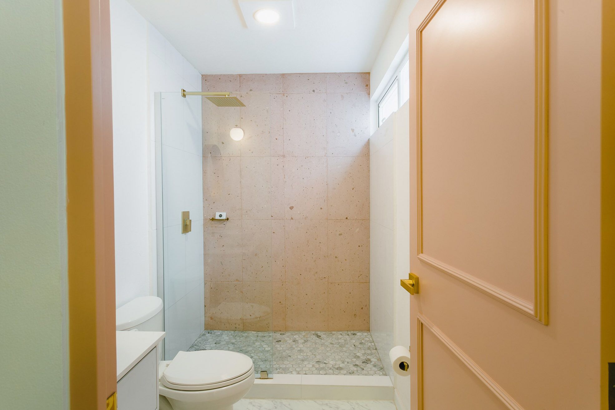 Um banheiro com vaso sanitário, chuveiro com porta de vidro e piso revestido de azulejos.