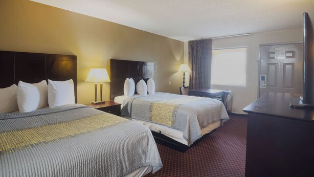 Quarto de hotel com duas camas, uma escrivaninha, uma televisão e uma janela.