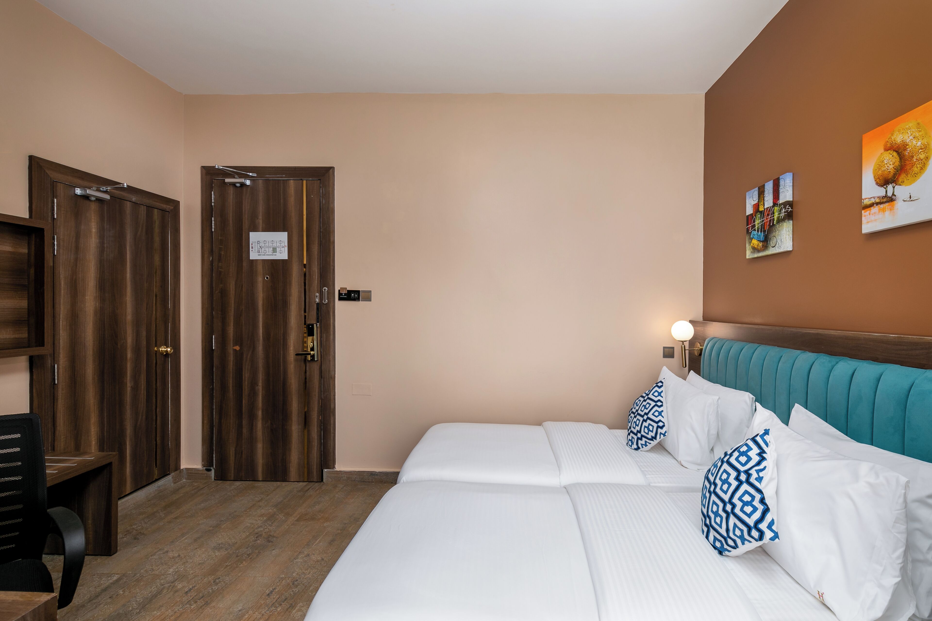 Quarto de hotel com cama, escrivaninha, cadeira e porta.