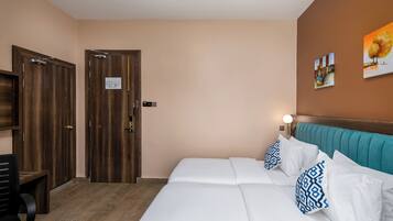 Quarto de hotel com cama, escrivaninha, cadeira e porta.