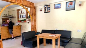Uma área de recepção com um arco de madeira, sofás de couro preto, uma mesa de madeira e um balcão de recepção com uma pessoa atrás.