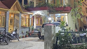 Um edifício com vários andares, varandas, área de recepção e veículos estacionados.
