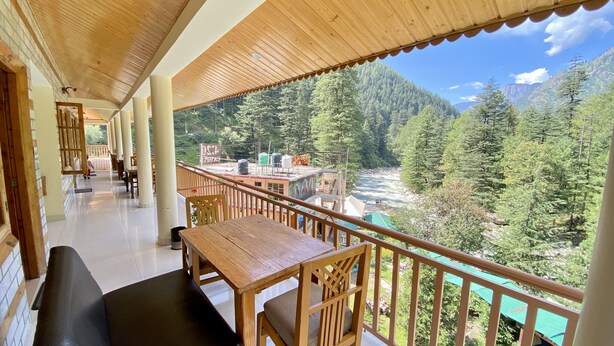 Um deck de madeira com uma mesa e cadeiras, com vista para um rio e montanhas arborizadas.