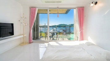 Quarto de hotel com cama, televisão, varanda com mesa e cadeiras e vista para o mar.