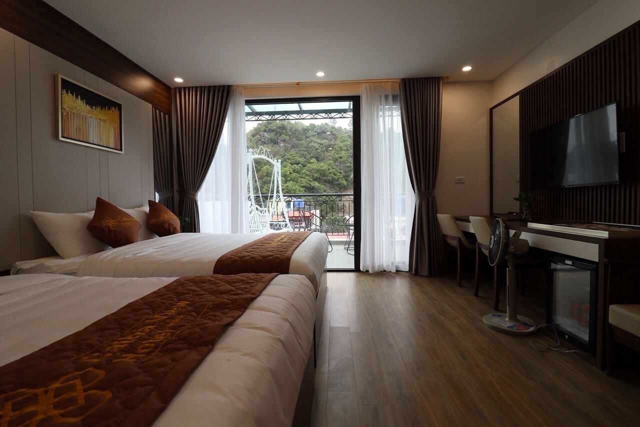 Quarto de hotel com duas camas, uma escrivaninha com televisão e varanda com vista para o verde.