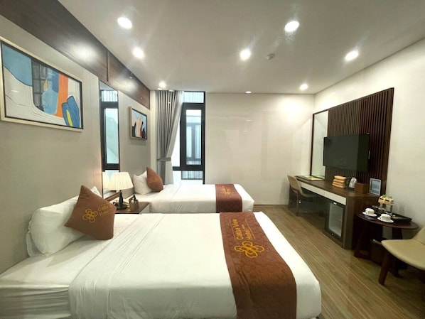 Quarto de hotel com duas camas, uma escrivaninha, televisão e janela com cortinas.
