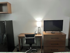 Um pequeno escritório com uma mesa, cadeira, TV e geladeira.
