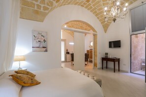 Quarto com cama grande, lustre, pintura e televisão na parede.