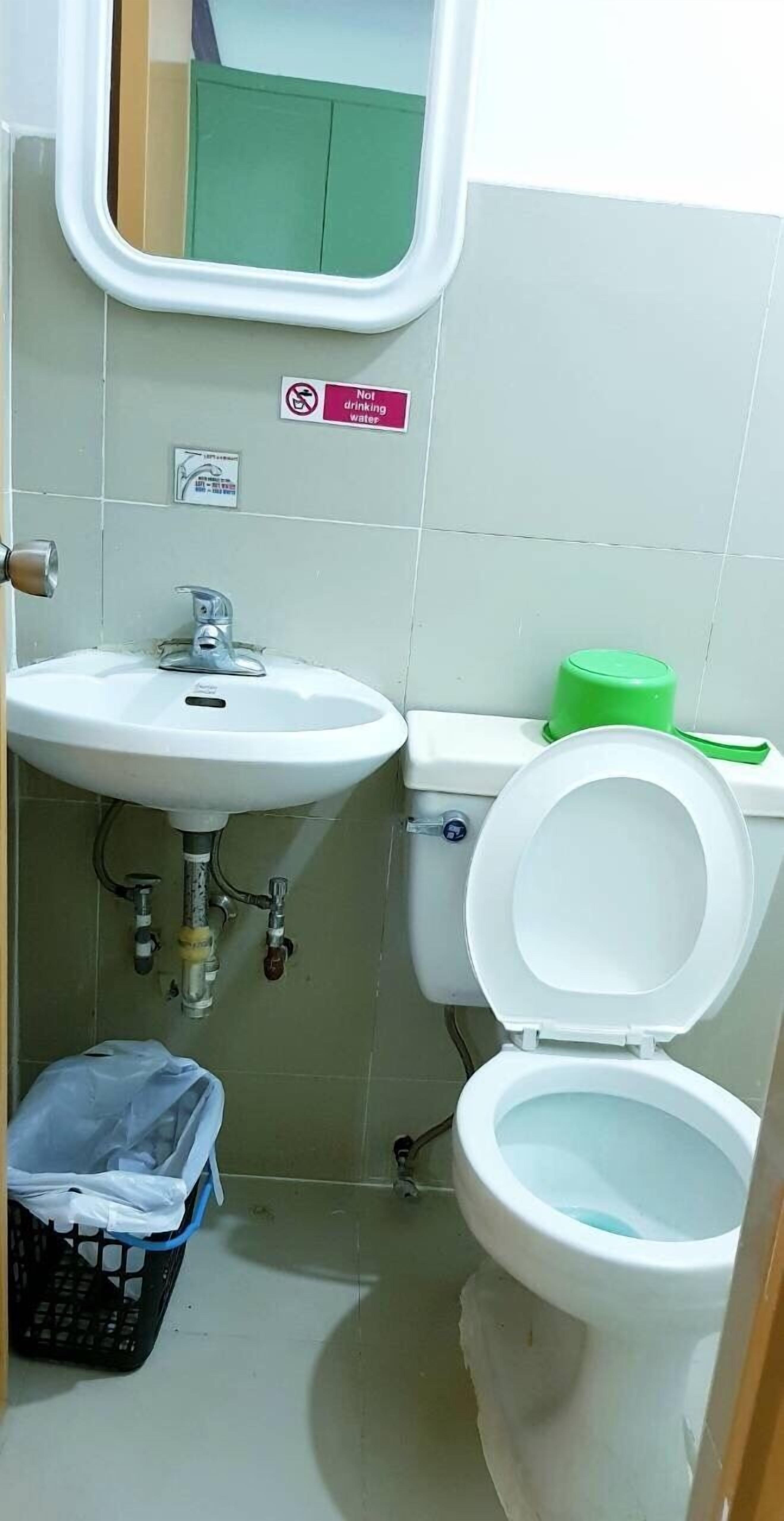 Casa de banho pequena com lavatório branco, sanita e um contentor de lixo verde.