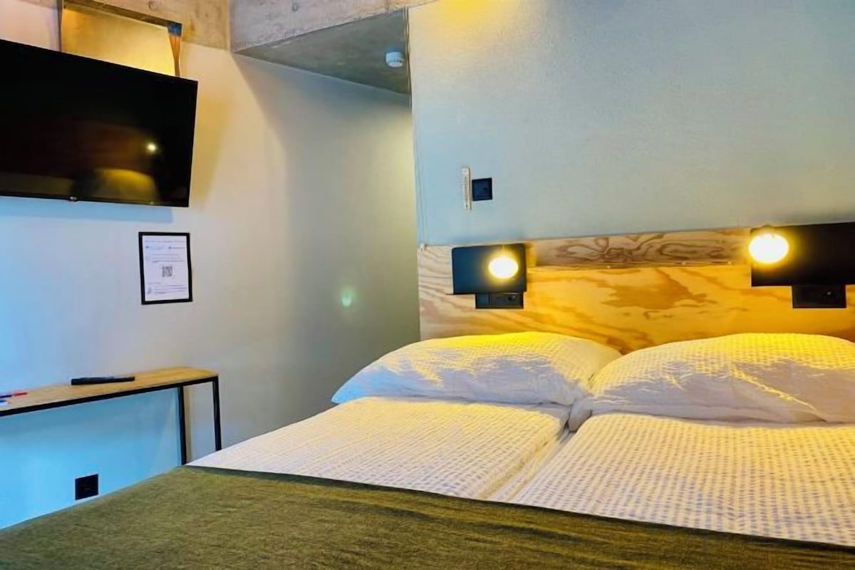 Quarto de hotel com cama, televisão de tela plana na parede e mesa de cabeceira.