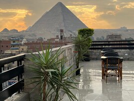Terraço no telhado com vista para uma pirâmide, plantas em vasos e móveis de exterior.