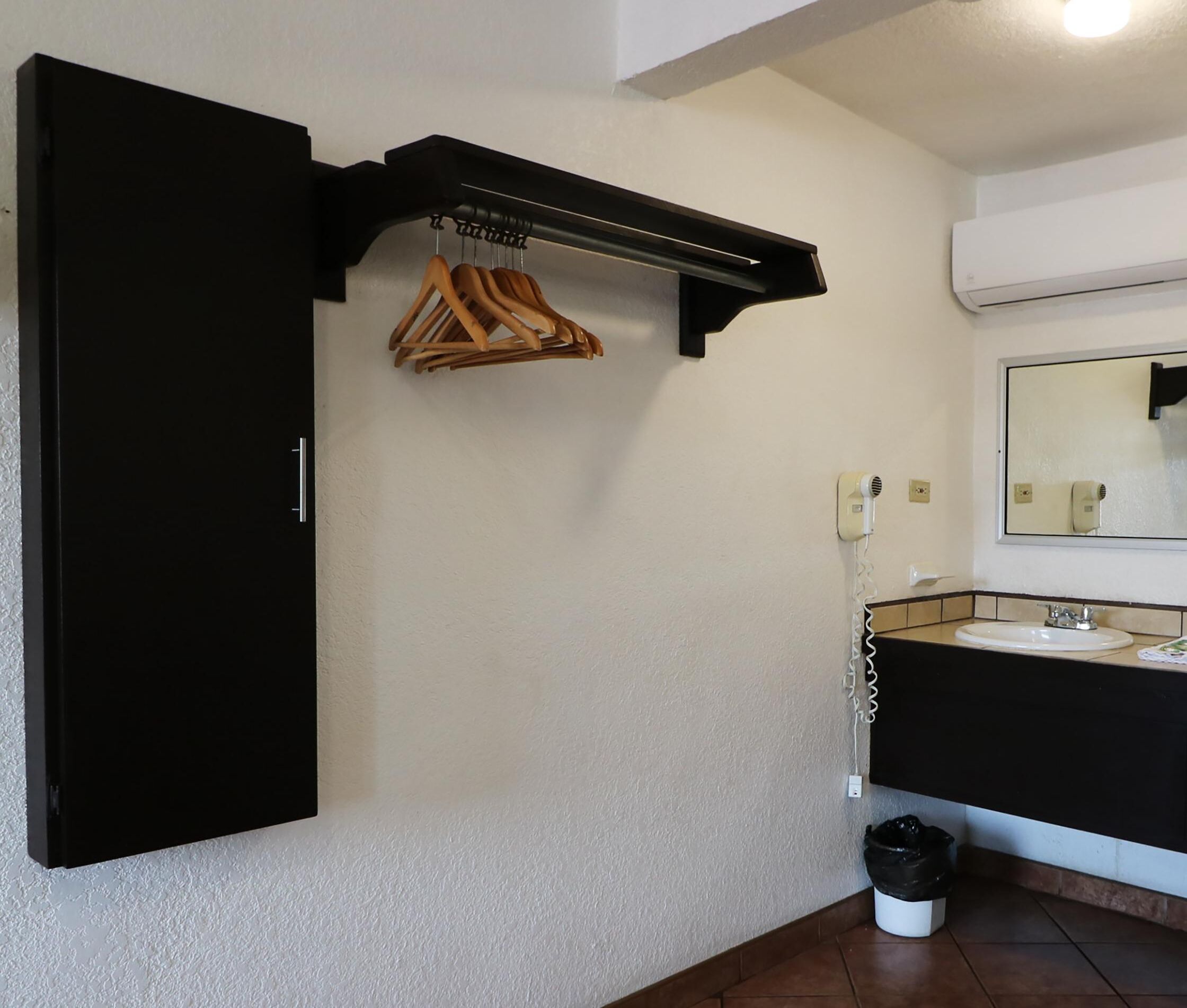 Um banheiro com um armário preto, um porta-toalhas com cabides de madeira, uma pia branca e um espelho.