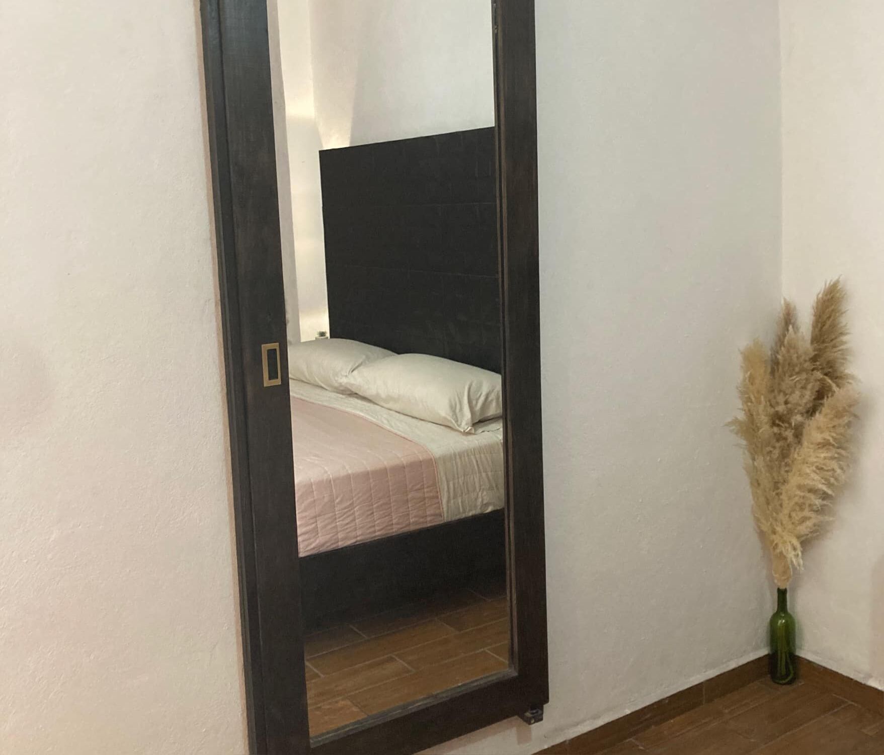 Quarto com cama, espelho e um vaso com plumas de lagos.