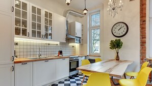 Uma cozinha moderna com armários brancos, piso xadrez, mesa de madeira e cadeiras amarelas.