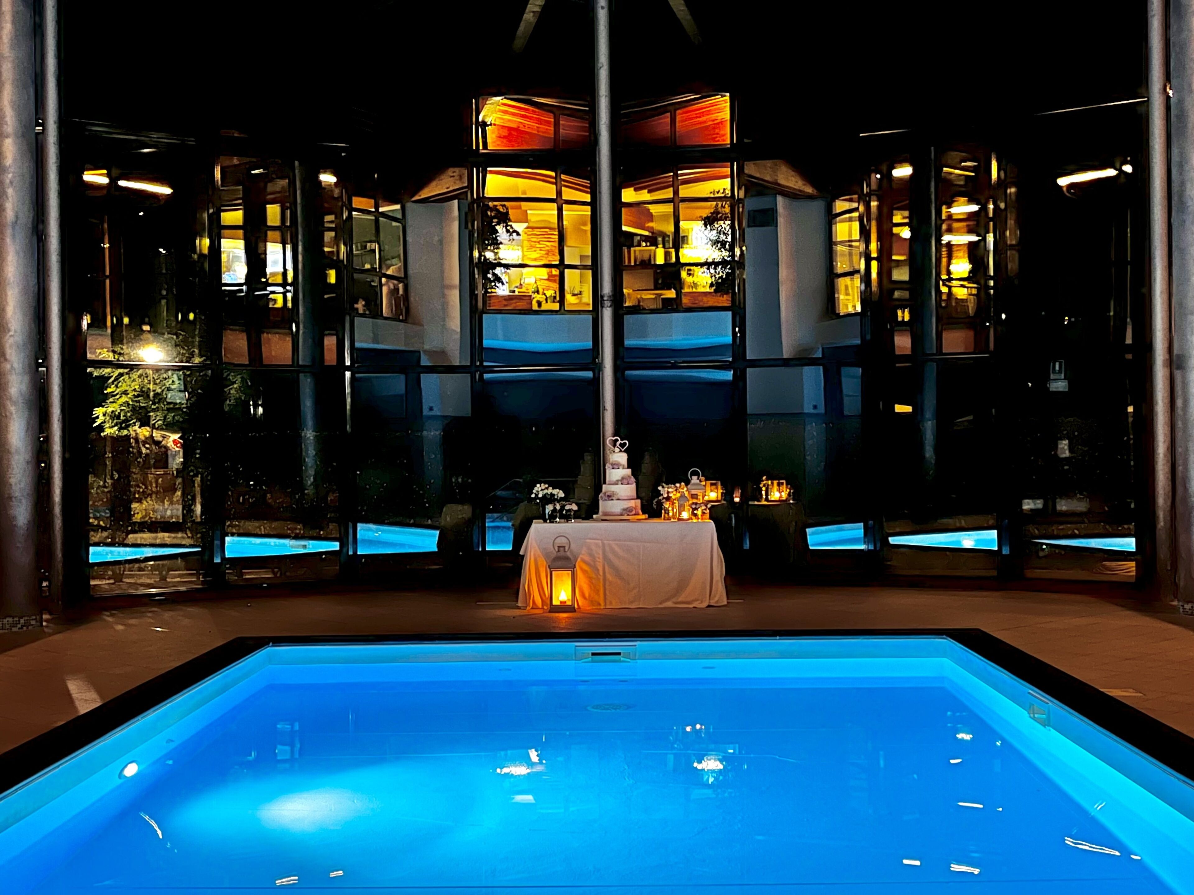 Piscina com mesa e cadeiras no centro, rodeada por paredes de vidro com iluminação interna.