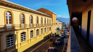 Um edifício amarelo com janelas e varandas arqueadas, uma rua com carros estacionados e um céu limpo.