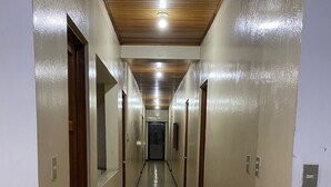 Um corredor comprido e estreito, com chão de azulejos e portas de madeira em ambos os lados.