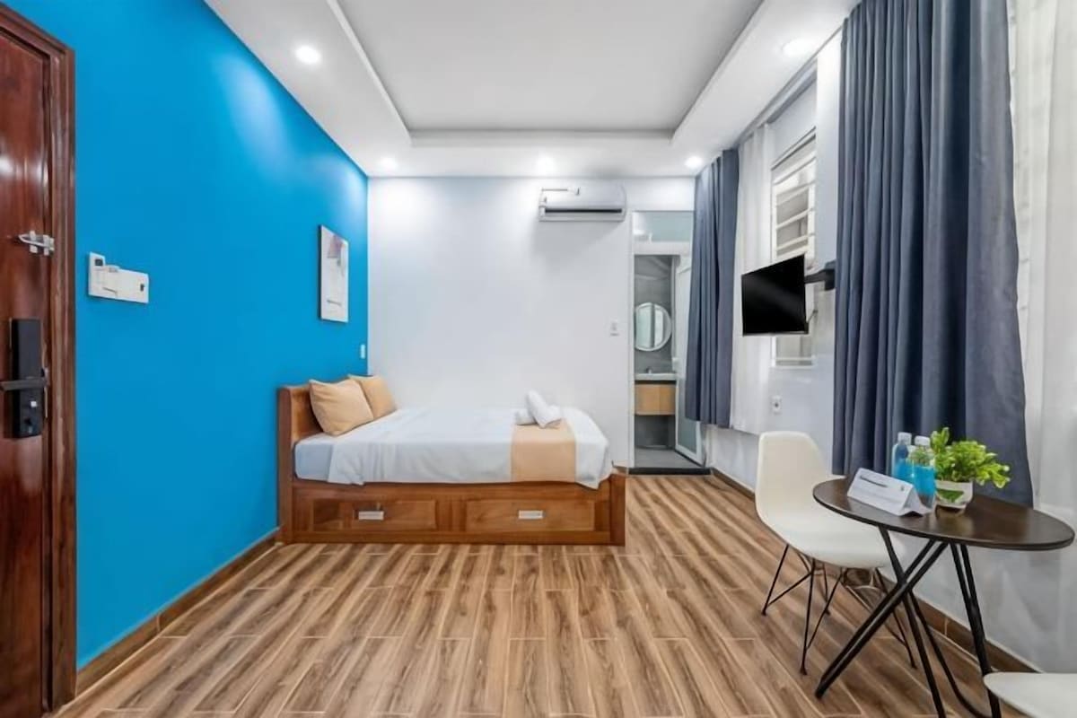 Quarto com cama, escrivaninha, cadeira e televisão.