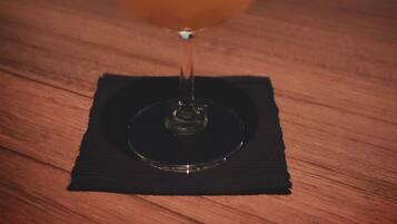 Um cocktail sobre uma mesa de madeira, com um fundo desfocado de uma piscina e iluminação interna.