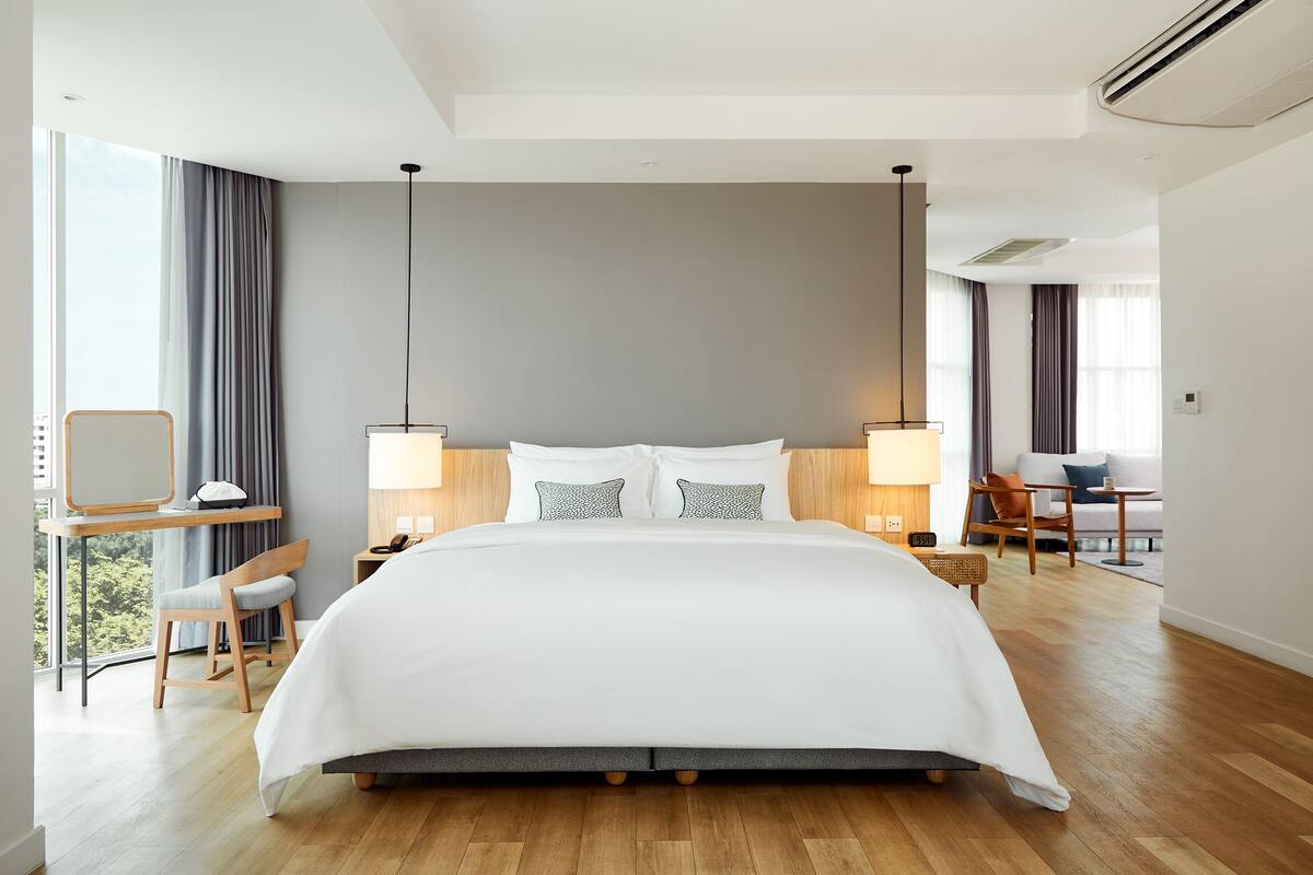 Quarto de hotel moderno com uma cama grande, piso de madeira e uma escrivaninha com cadeira.