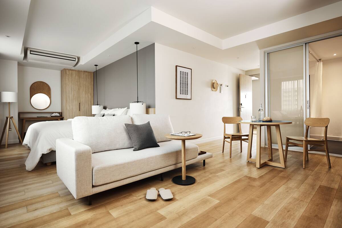 Quarto de hotel moderno com sofá, mesa redonda pequena, uma cadeira, cama e um espelho grande.