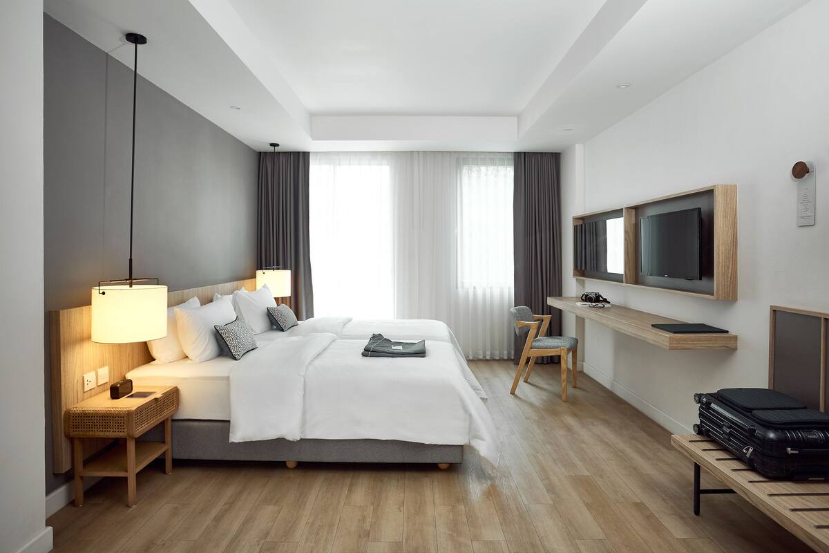 Quarto de hotel moderno com uma cama grande, uma escrivaninha, uma televisão e uma mala em um banco.