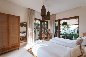 Quarto com duas camas, guarda-roupa de madeira, mesa com cadeiras e vista para o exterior.
