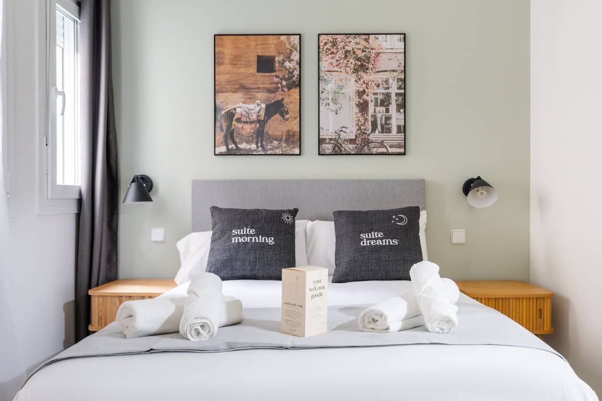 Uma cama bem arrumada com duas almofadas, uma mesa de cabeceira e duas luminárias na parede.