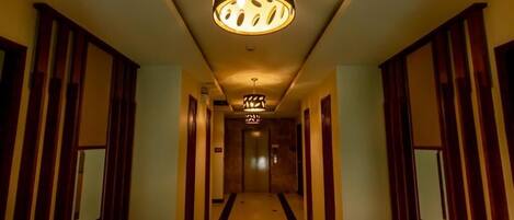 Corredor de hotel com painéis de madeira, luminária central e extintor de incêndio à direita.