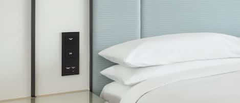 Quarto de hotel moderno com uma cama grande, uma mesinha de cabeceira, um painel de controle na parede e uma luminária pendente.