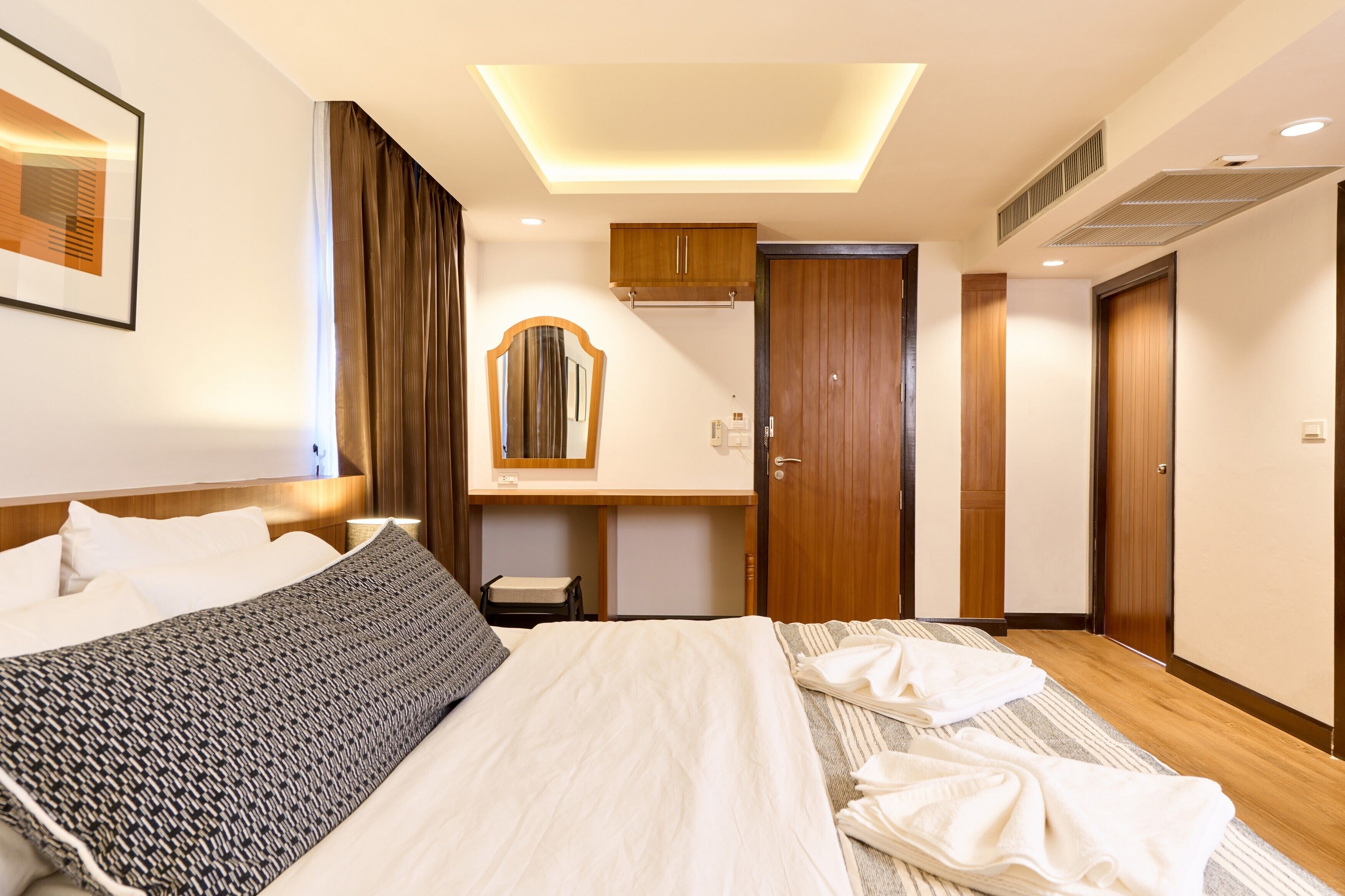Quarto de hotel com cama, mesa de cabeceira, espelho, guarda-roupa e uma lâmpada no teto.