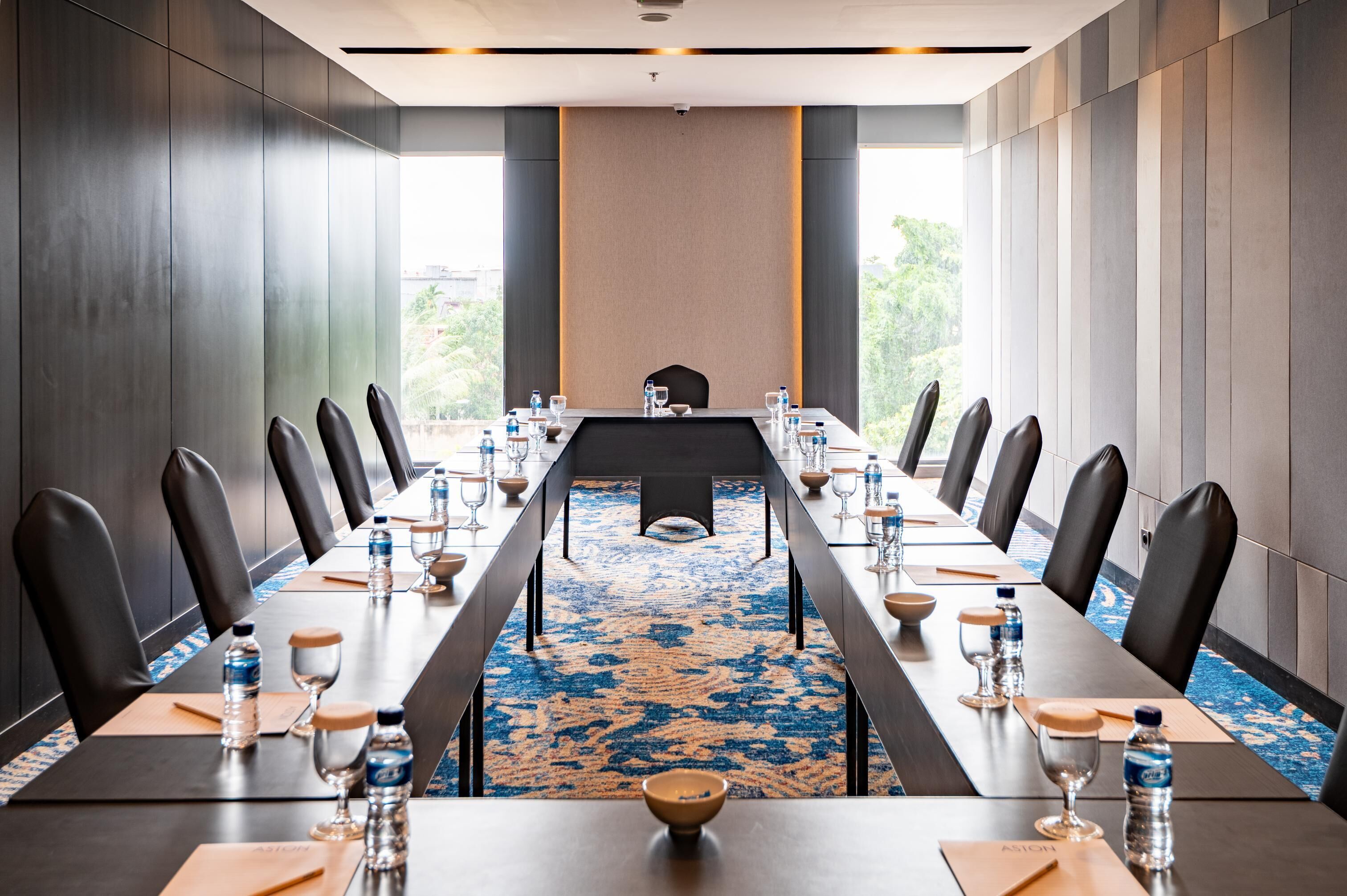 Uma sala de conferências com uma mesa comprida, cadeiras, garrafas de água e copos.