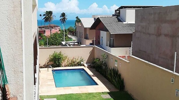Quintal residencial com piscina, gramado bem cuidado e vista para o oceano.