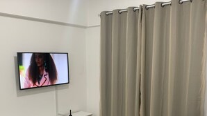 Uma sala de estar moderna com televisão de tela plana na parede, um sofá cinza, um móvel branco com espaço para guardar coisas e cortinas finas na janela.