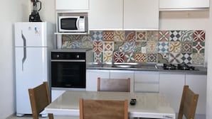 Cozinha compacta com armários brancos, micro-ondas, fogão a gás e geladeira. Há uma mesa de jantar com quatro cadeiras.