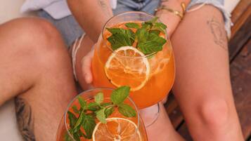 Duas pessoas segurando copos com bebidas e fatias de cítricos e folhas de hortelã.