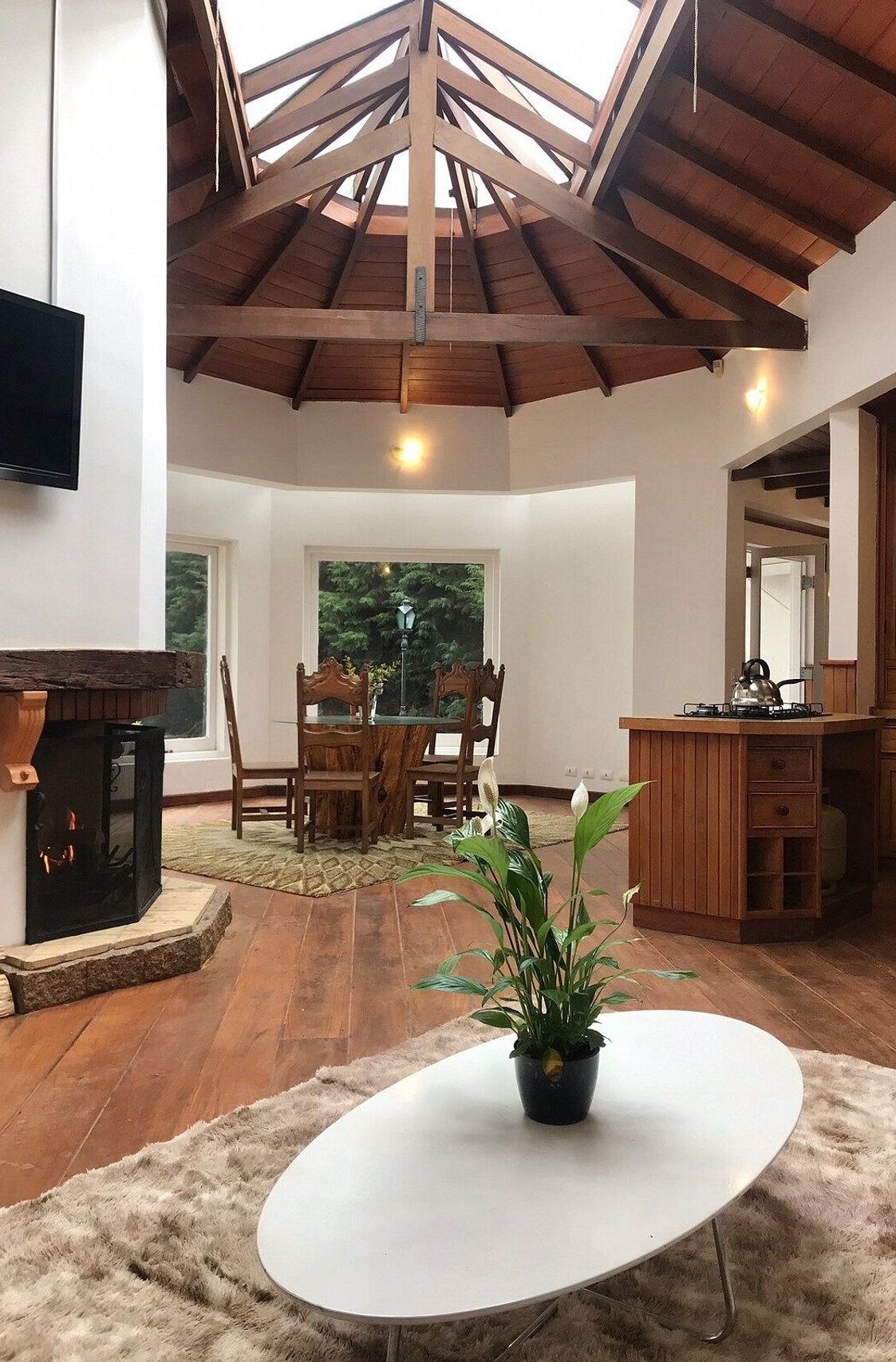 Uma sala de estar ampla com pé direito alto, lareira, mesa de jantar e área de cozinha.