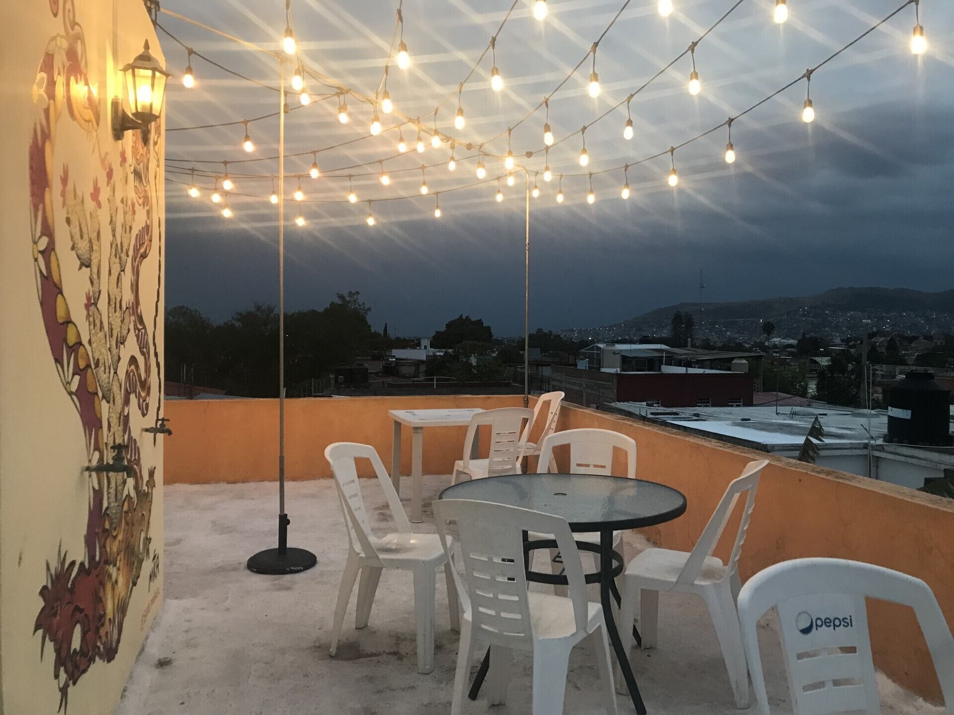 Um pátio externo com luzes de Natal, cadeiras de plástico branco e uma mesa.