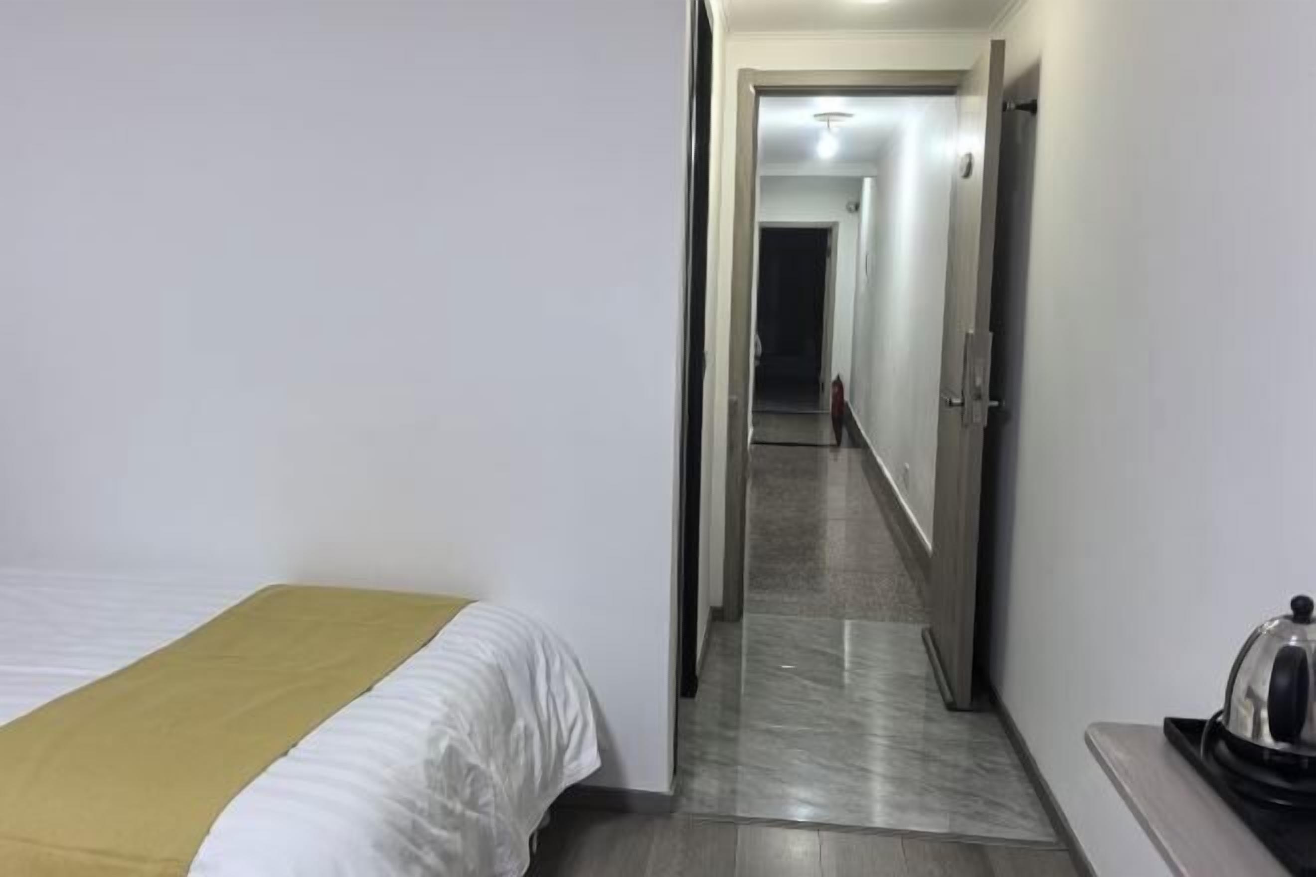 Quarto de hotel com uma cama, uma mesa de cabeceira e uma chaleira sobre a mesa.