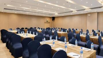 Sala de conferências com fileiras de mesas e cadeiras, equipada com garrafas de água e placas de identificação.