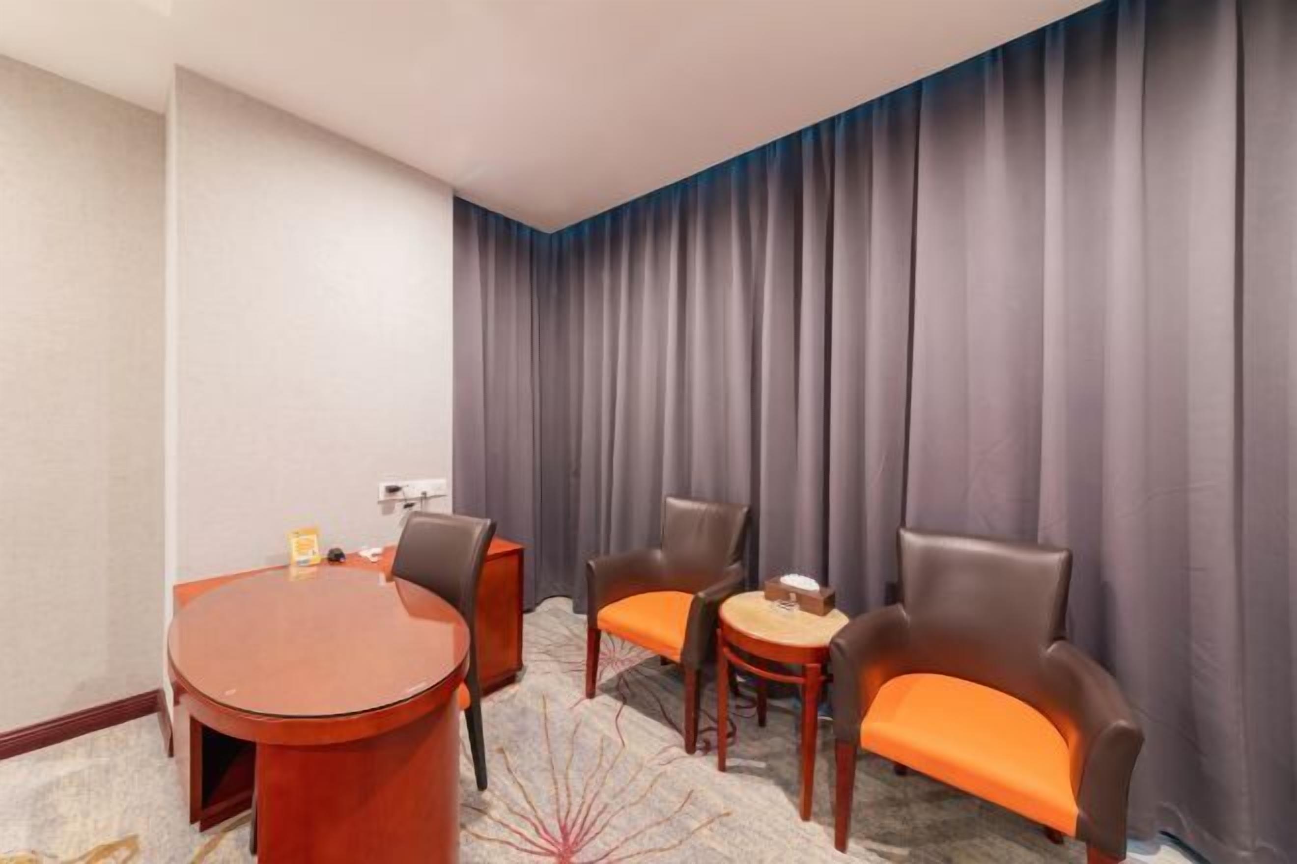 Quarto de hotel com uma mesa redonda de madeira, duas poltronas de couro e uma pequena mesa redonda com uma cadeira.