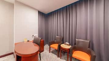 Quarto de hotel com uma mesa redonda de madeira, duas poltronas de couro e uma pequena mesa redonda com uma cadeira.