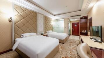 Quarto de hotel com duas camas, uma escrivaninha, uma televisão e um espelho.