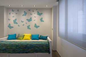Quarto com cama, almofadas coloridas, manta estampada e adesivos de borboletas na parede.